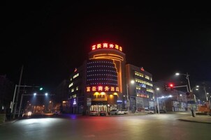 Um hotel com uma placa vermelha grande na parte superior, vários andares e um estacionamento em frente.
