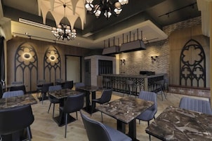 Interior de restaurante com mesas de mármore, cadeiras pretas e arandelas decorativas.