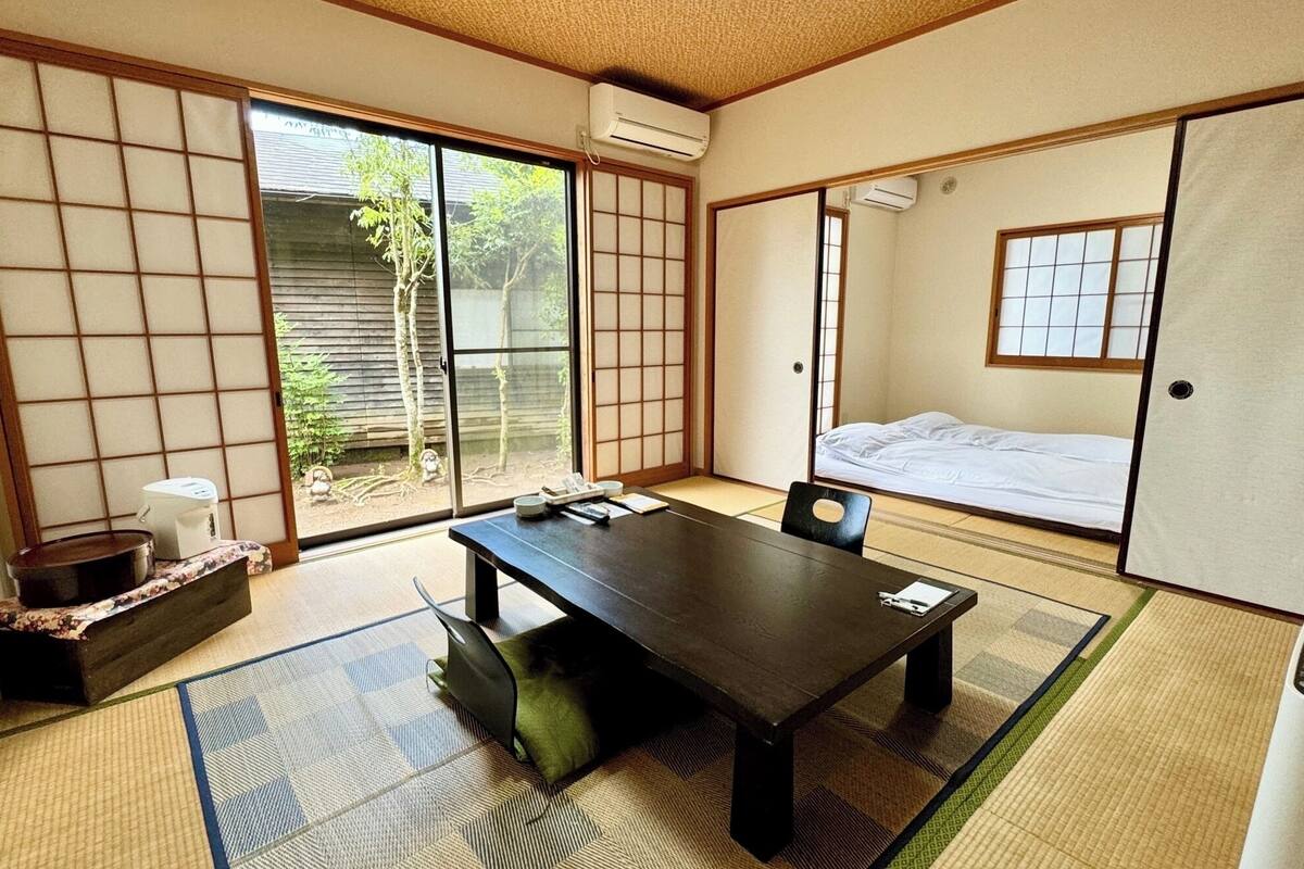 Um quarto japonês tradicional com tatames, uma porta deslizante, uma cama e uma mesa com uma cadeira.