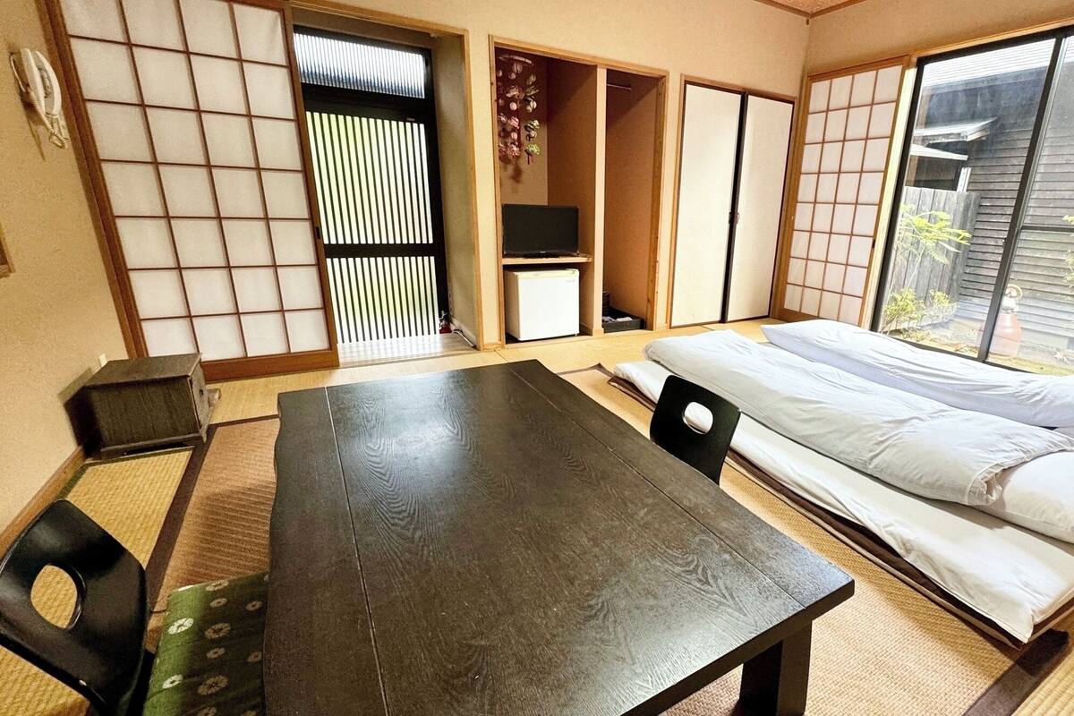 Um quarto japonês tradicional com tatames, futon, mesa baixa e portas deslizantes.