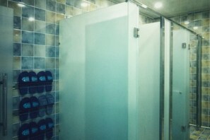 Casa de banho com chuveiro em cabine de vidro e parede revestida em azulejos, incluindo um sapateiro.