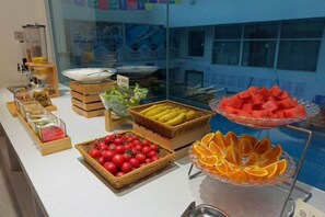 Buffet com diversos alimentos, incluindo tomates, bananas, melancia e laranjas.
