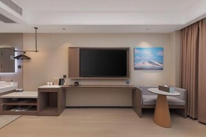 Quarto de hotel moderno com televisão de tela plana, sofá, mesa de centro, escrivaninha e uma janela grande.