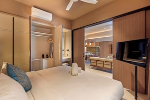 Quarto de hotel moderno com uma cama grande, televisão, guarda-roupa e porta aberta para uma área de jantar.