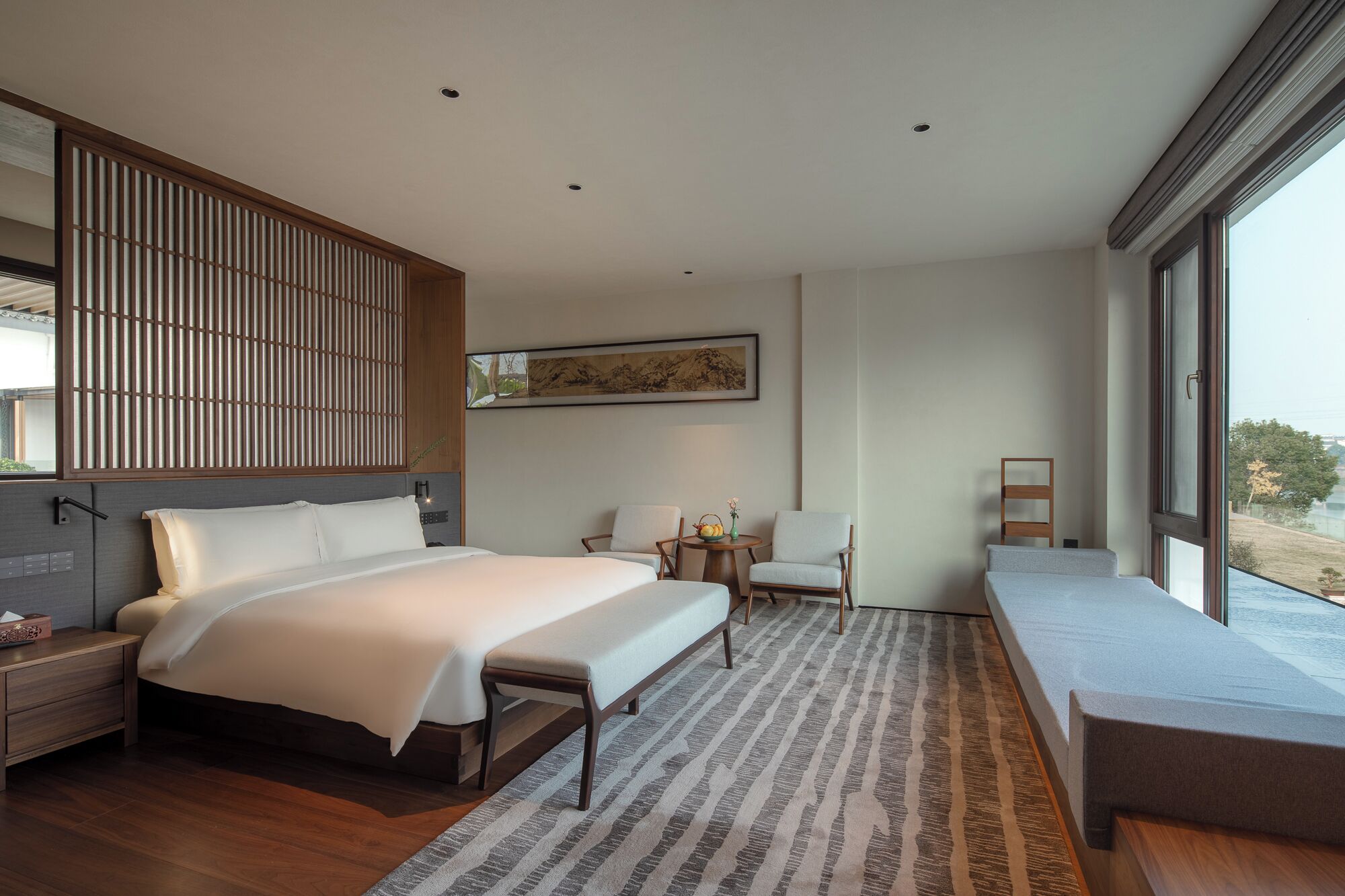 Quarto de hotel moderno com uma cama grande, área de estar com uma mesinha, uma janela ampla e vista para o exterior.