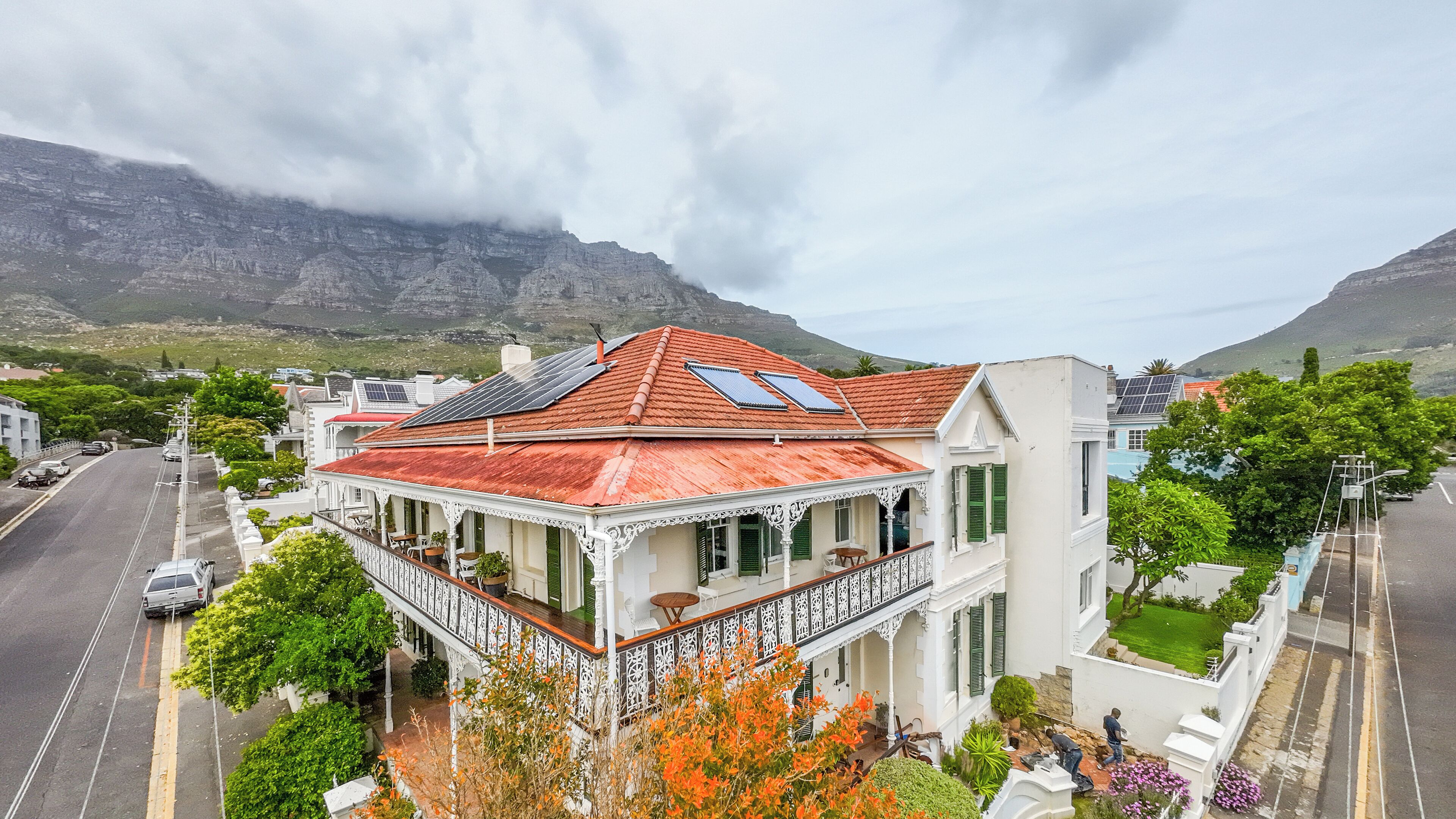 Um edifício em estilo colonial com telhado de telhas vermelhas, paredes brancas e uma varanda com grades ornamentadas.