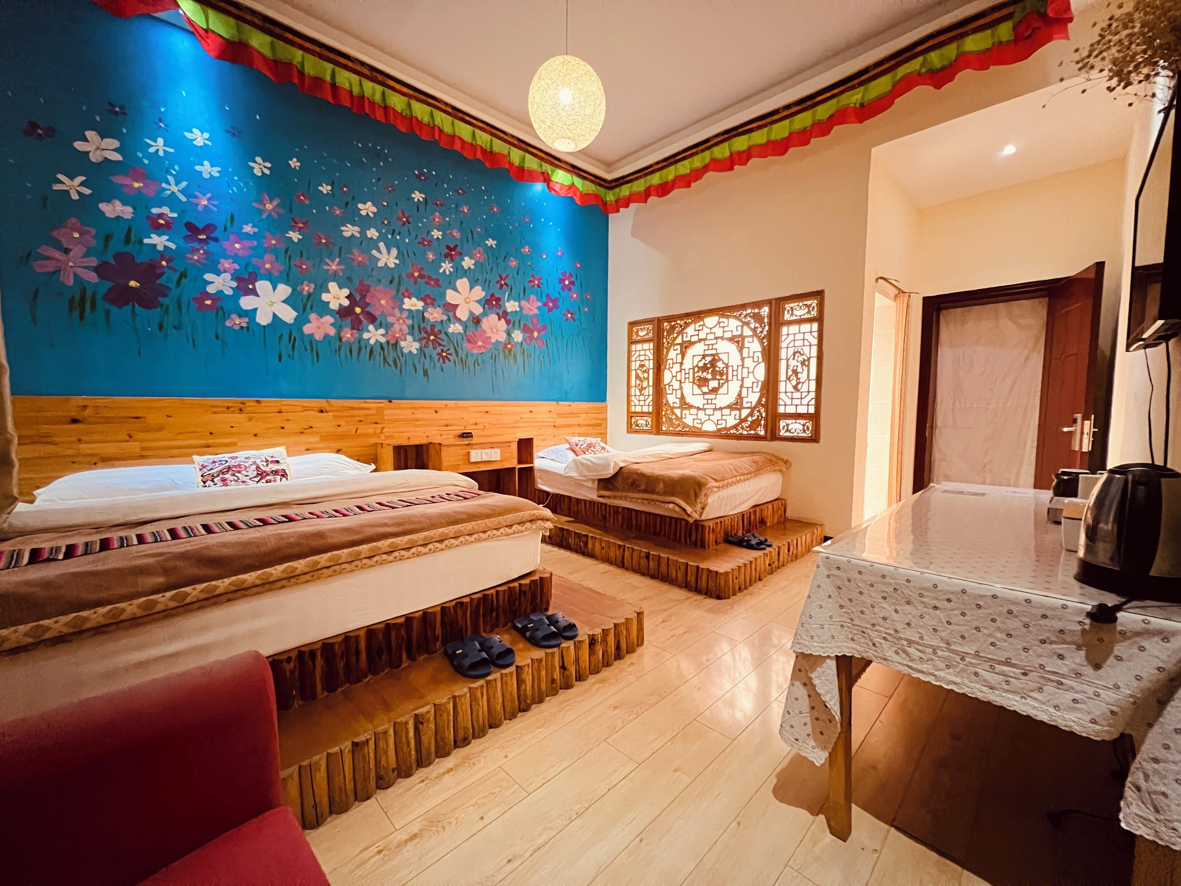 Quarto de hotel com duas camas, piso de madeira, parede decorativa com motivos florais e um divisório de estilo tradicional.