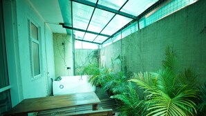 Um quarto com uma mesa de madeira e cadeiras, uma banheira branca e plantas verdes exuberantes.