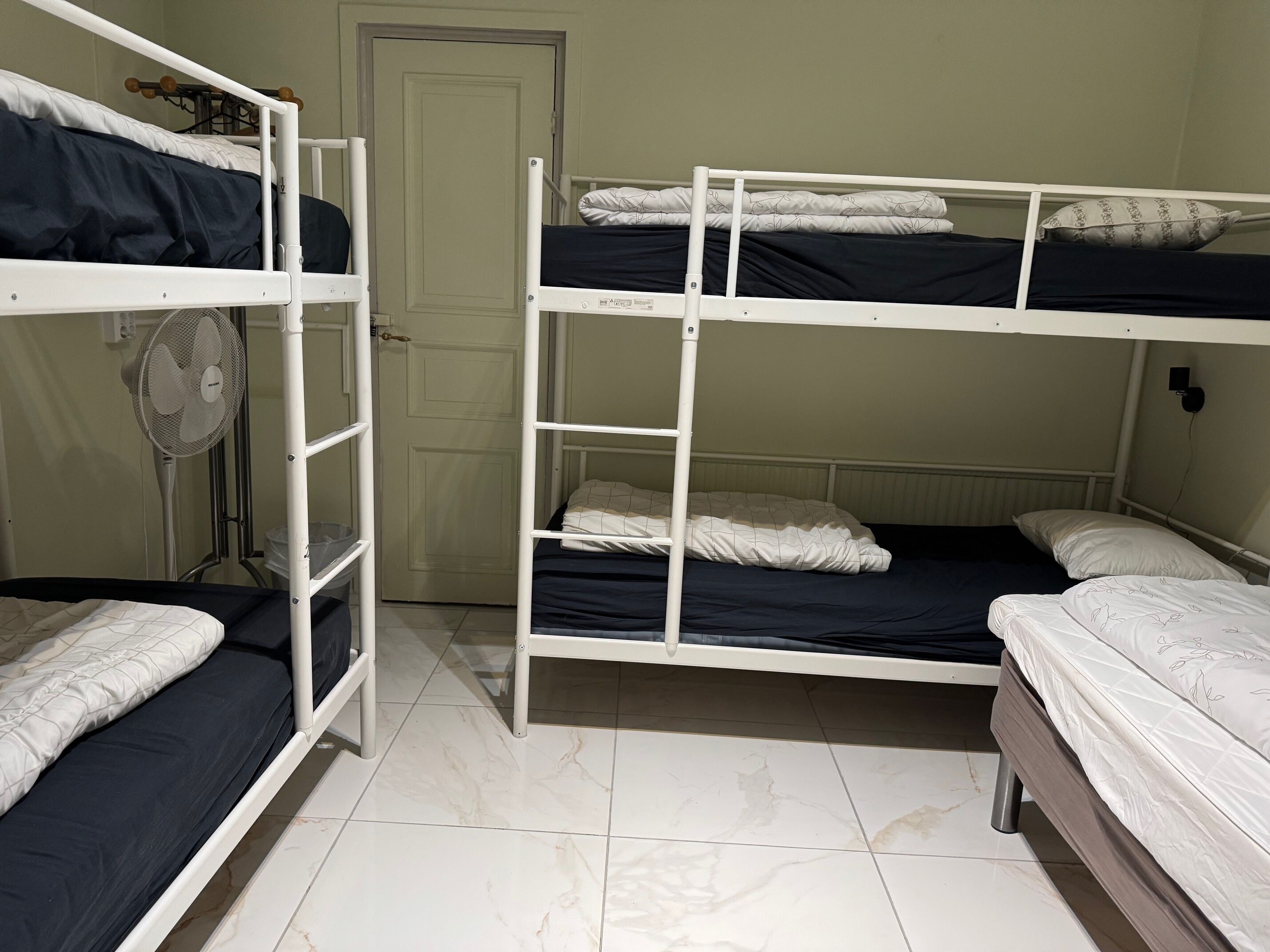 Um dormitório com beliches, um ventilador e uma porta.