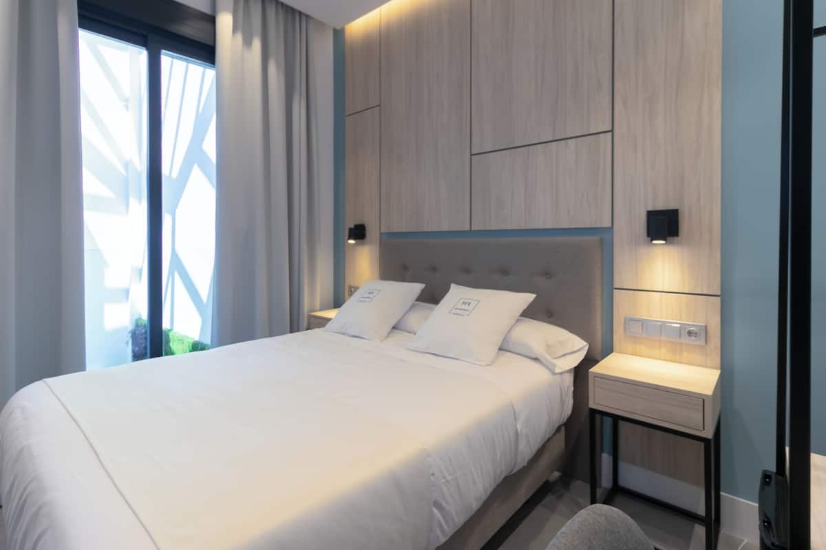Quarto de hotel moderno com uma cama grande, cabeceira de madeira e mesas de cabeceira com luminárias.