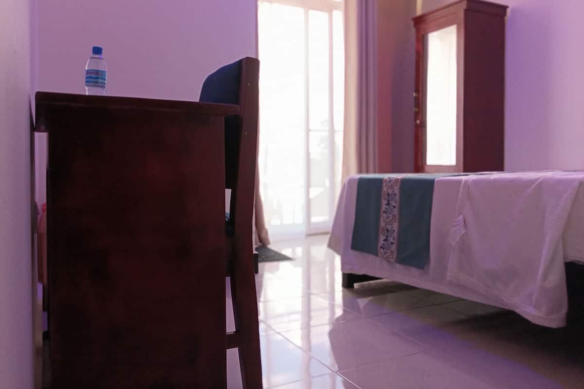 Quarto com cama, uma cadeira de madeira, uma garrafa de água sobre a cadeira e um armário.