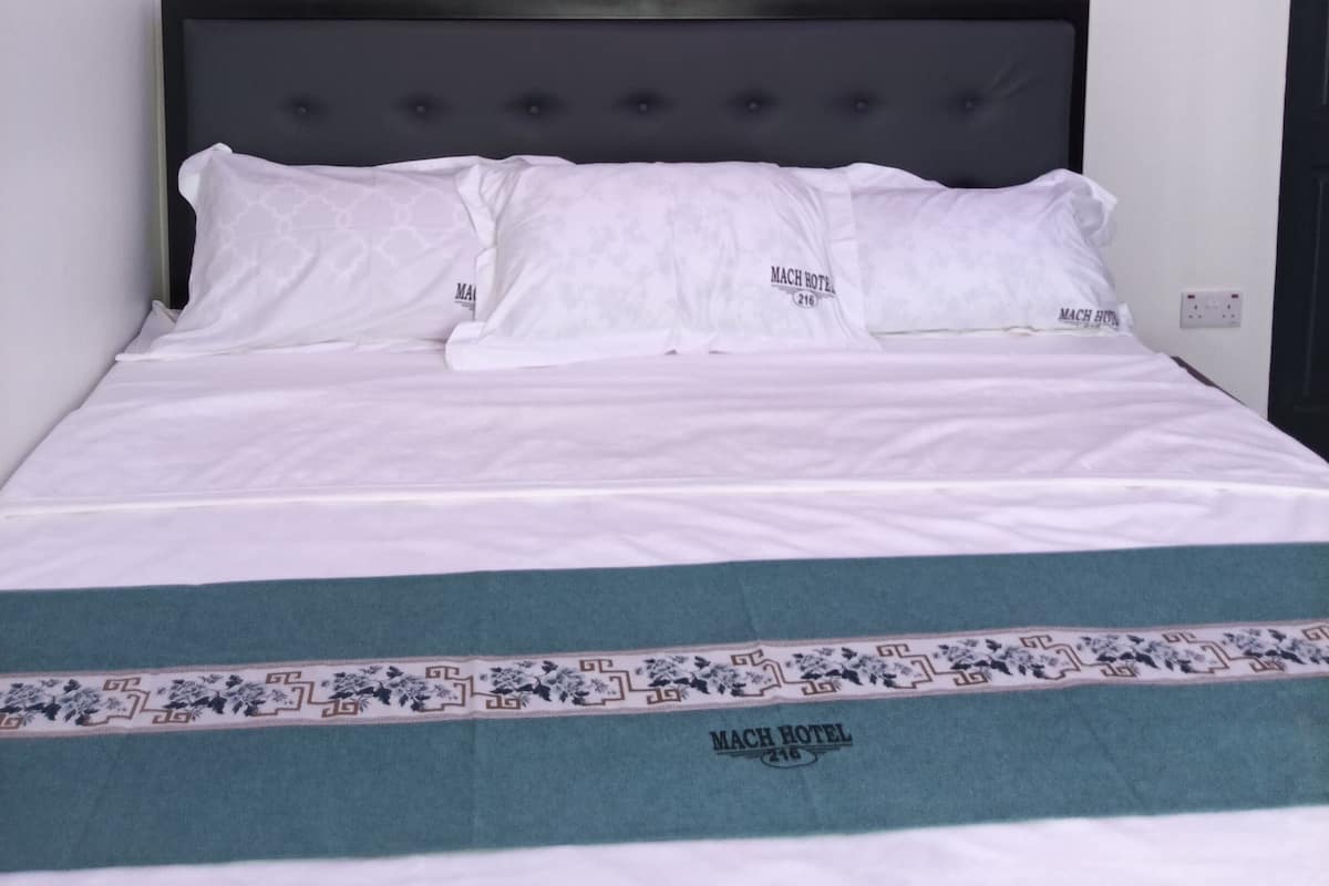 Uma cama com cabeceira escura, roupa de cama branca e bordado decorativo.