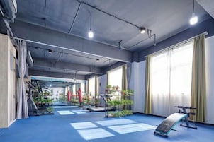 Academia com equipamentos de ginástica, grandes janelas e piso azul.