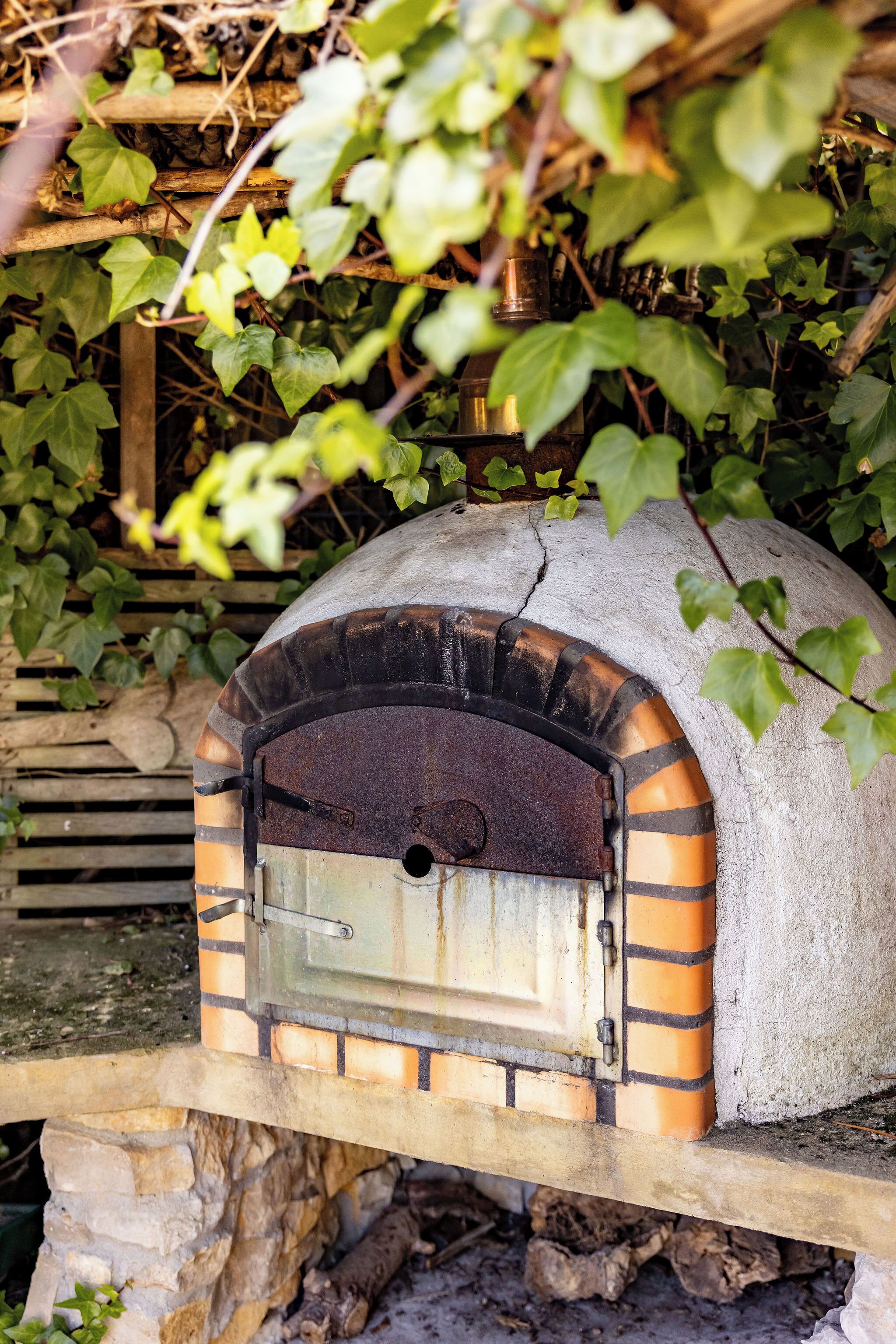 Forno de pedra com interior de tijolos, rodeado por vegetação.