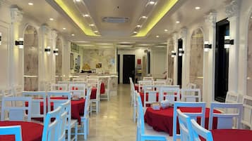 Espaço de refeições de hotel com cadeiras brancas, toalhas de mesa vermelhas, piso de mármore e design de teto moderno.