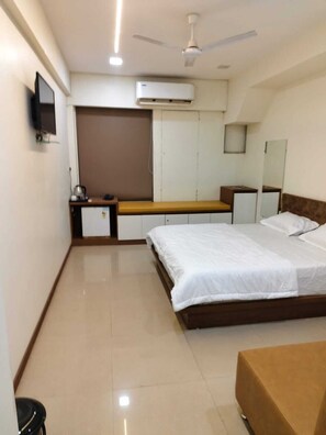 Quarto de hotel com cama, escrivaninha, cadeira, televisão, ar condicionado e ventilador de teto.
