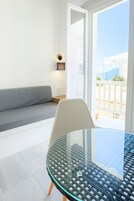 Quarto moderno com mesa de vidro, sofá cinzento e varanda com vista.