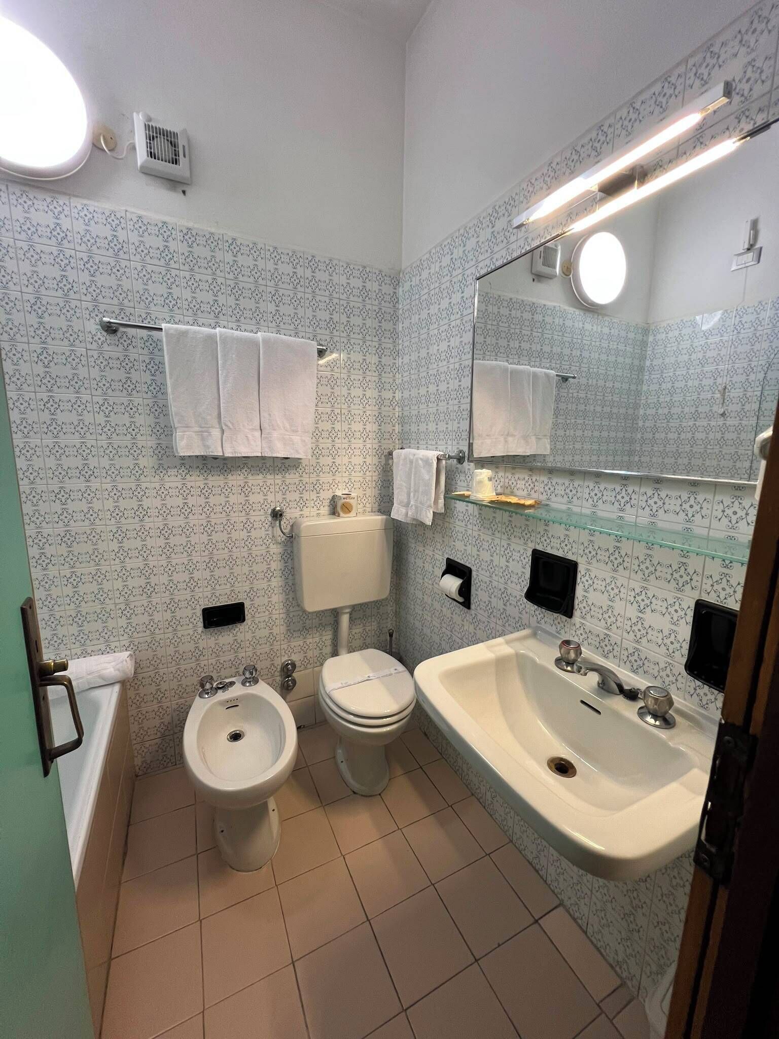 Casa de banho com sanita, bidé, lavatório e espelho iluminado.