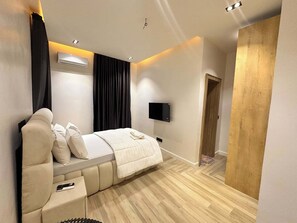 Quarto moderno com cama, televisão e porta de madeira.