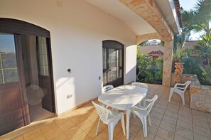 Um pátio com uma mesa e cadeiras brancas, uma porta e um muro de pedra com uma estátua.