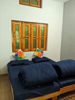 Quarto com cama de madeira, duas almofadas coloridas e porta de madeira com painéis de vidro.