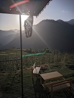 Um banco e uma mesa de madeira sob uma pérgula, com vista para um vinhedo e montanhas ao longe.
