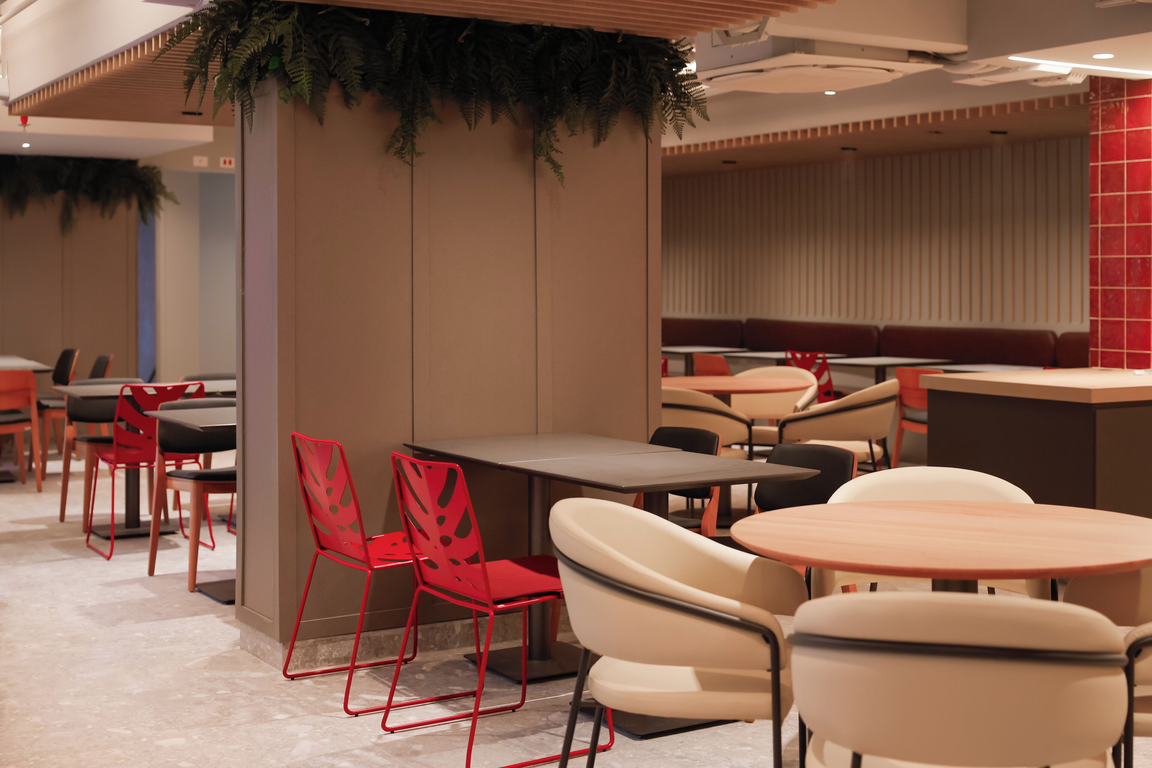 Um restaurante moderno com várias mesas e cadeiras, incluindo assentos vermelhos e bege.