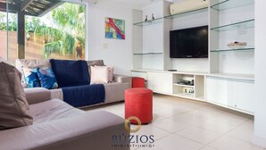 Uma sala de estar moderna com sofá, apoio para os pés, estantes de vidro e televisão.