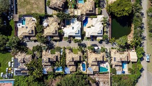 Vista aérea de um resort com vários edifícios no estilo de bangalôs, cada um com piscina privativa e cercado por vegetação exuberante.
