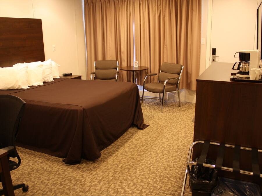 Quarto de hotel com cama grande, duas poltronas, mesa pequena com cafeteira e escrivaninha.