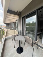 Uma varanda moderna com uma mesa redonda e cadeiras, uma porta de vidro que dá para uma sala de jantar, e vista para a paisagem urbana.