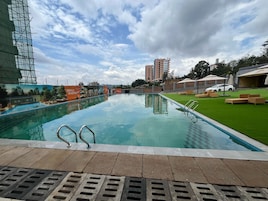 Piscina com padrão quadriculado, cercada por gramado e espreguiçadeiras.