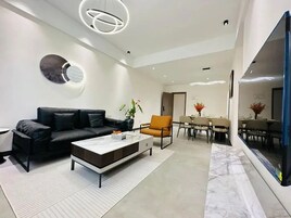 Uma sala de estar moderna com um sofá de couro preto, uma mesa de centro branca e uma área de jantar com mesa e cadeiras.