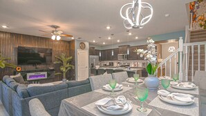 Uma sala de estar moderna com sofá, mesa de jantar para quatro pessoas e cozinha ao fundo.