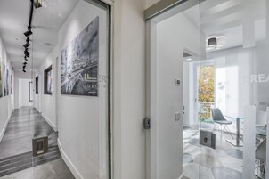 Um corredor de hotel moderno com uma porta de vidro que dá para uma área de refeições, uma fotografia em preto e branco na parede, e um design limpo e minimalista.