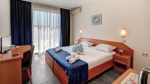 Quarto de hotel com cama, mesas de cabeceira, escrivaninha com computador, cadeira e janela com cortinas.