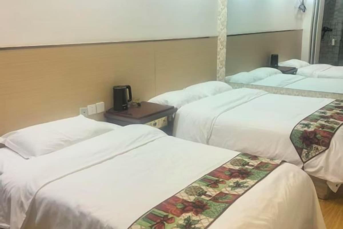 Quarto de hotel com duas camas, cada uma com colcha branca e edredom decorativo. Há uma mesa de cabeceira com cafeteira e luminária.