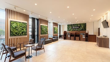 Um saguão moderno de hotel com balcão de recepção, área de estar e grandes janelas.