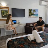 Quarto de hotel com cama, escrivaninha com laptop, televisão e sofá.