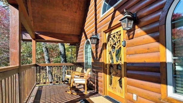 Uma cabana de madeira com varanda coberta, porta decorativa e janela.