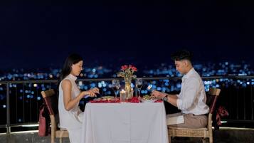 Um casal jantando em mesa externa com vista para a cidade à noite.