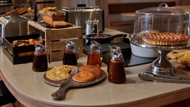 Um buffet de café da manhã com diversos pães, uma chapa quente e acompanhamentos.