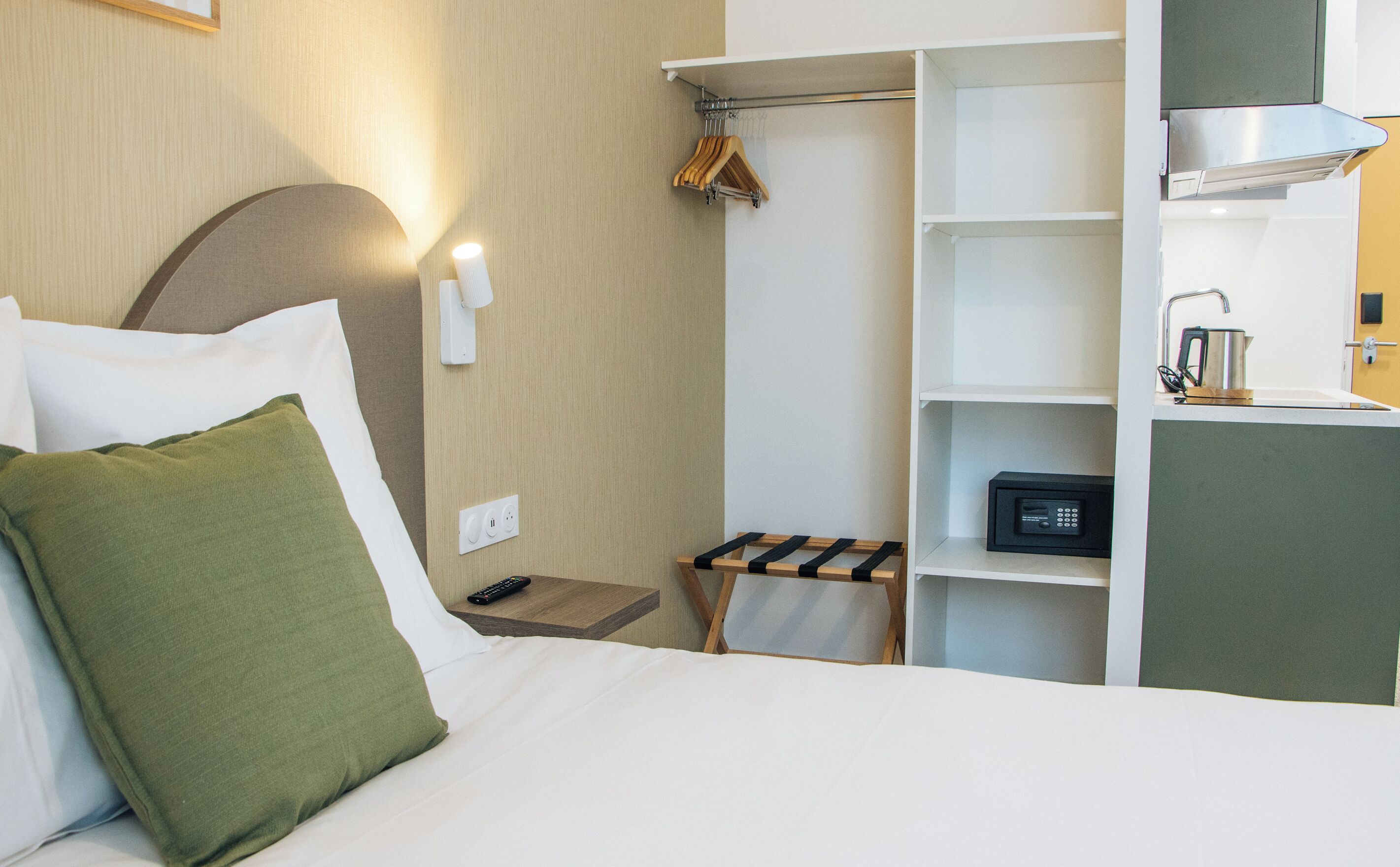 Quarto de hotel com cama, mesa de cabeceira, mesinha, cabideiro, micro-ondas e pia.