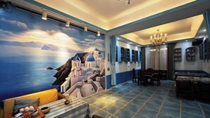 Quarto com um mural representando uma paisagem costeira, área de jantar com mesa e cadeiras, e um lustre.