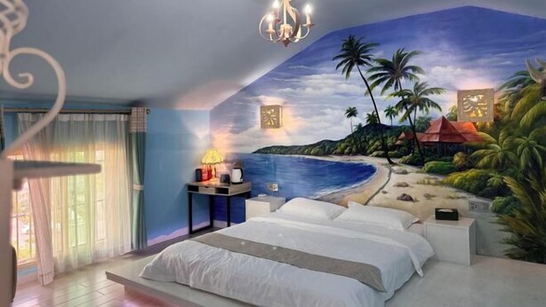 Quarto com mural de uma praia, cama, mesas de cabeceira e um lustre.