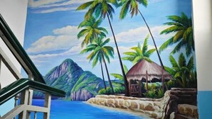 Cena de praia tropical com palmeiras, um bangalô de palha e um muro de pedra.