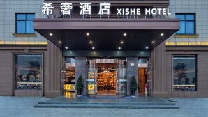 Exterior do HOTEL XISHE, com fachada moderna, ampla entrada de vidro e sinalização iluminada.