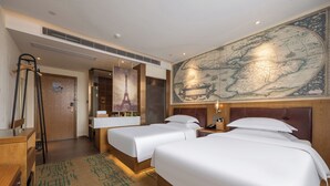 Quarto de hotel com duas camas, um mapa-múndi grande na parede, cabeceira de madeira e uma pequena mesa com luminária.