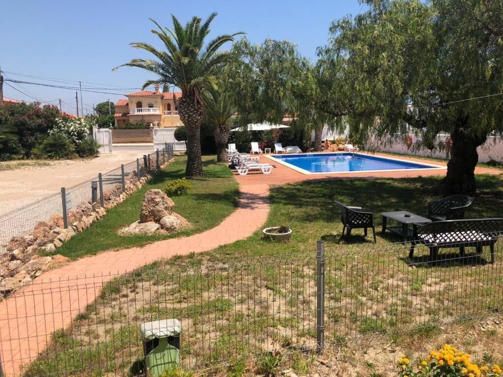 Quintal com piscina, cadeiras de descanso e área cercada com um banco.