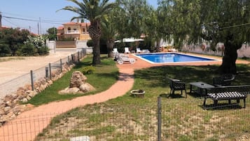 Quintal com piscina, cadeiras de descanso e área cercada com um banco.